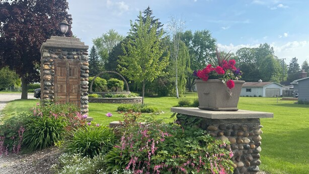 Um jardim com uma fonte de pedra, um muro de pedra e diversas plantas e flores.