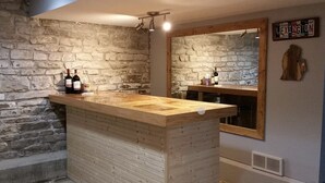 Uma área de bar com bancada de madeira, paredes de pedra e um espelho refletindo o ambiente.