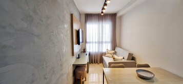 Uma sala de estar moderna com um sofá, uma mesa de jantar e uma TV fixada na parede.