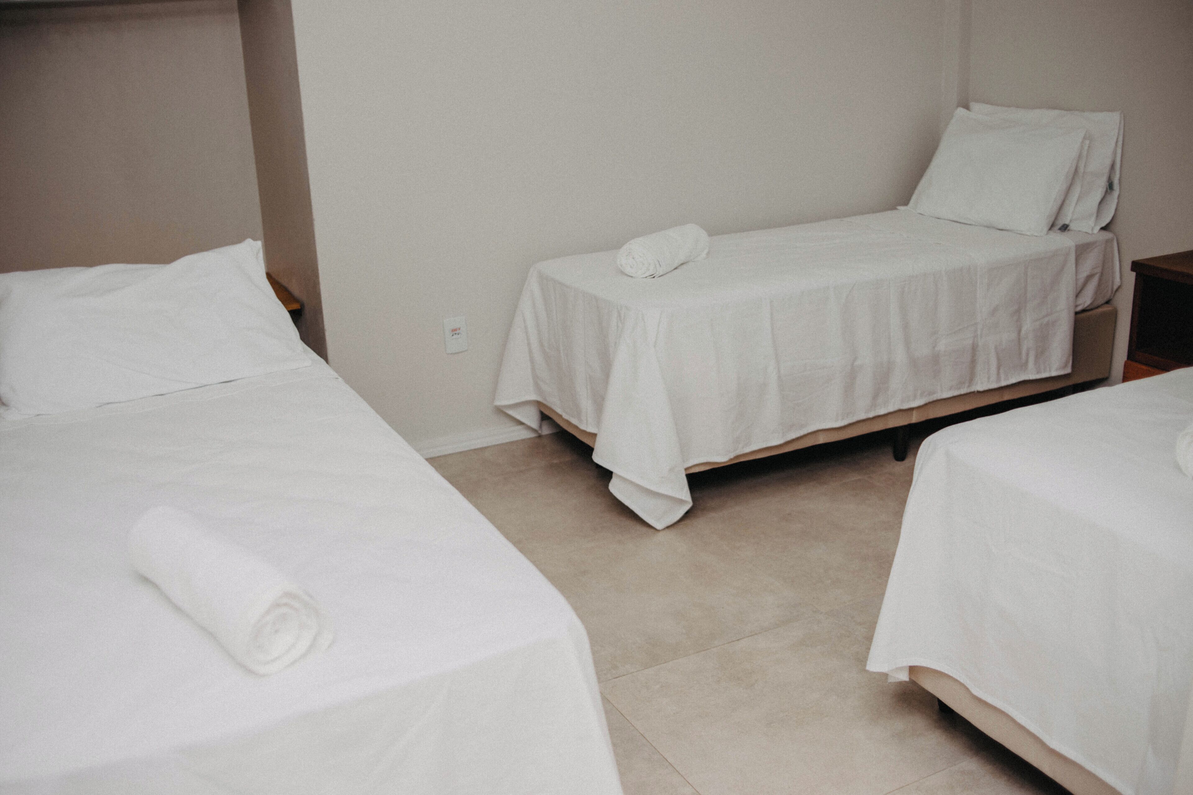 Quarto de hotel com duas camas de solteiro, cada uma com colcha e almofadas brancas.