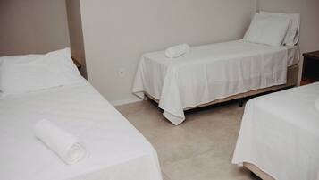 Quarto de hotel com duas camas de solteiro, cada uma com colcha e almofadas brancas.