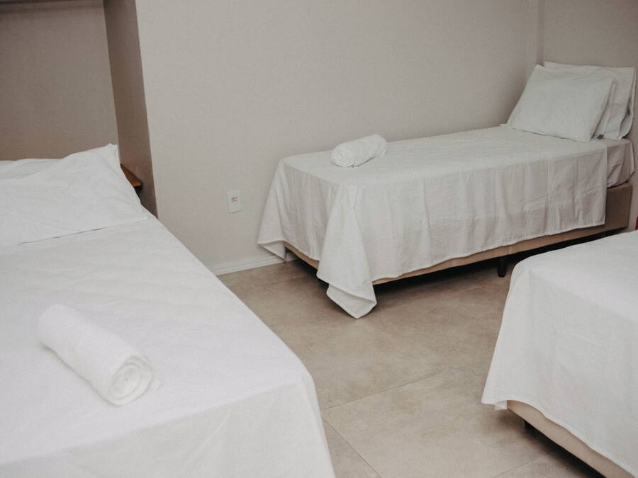 Quarto de hotel com duas camas de solteiro, cada uma com colcha e almofadas brancas.