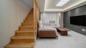Uma sala de estar moderna com escada de madeira, um sofá, uma mesa de centro e uma TV de tela plana na parede.