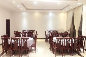 Uma sala de jantar com várias mesas e cadeiras, um lustre e cortinas.