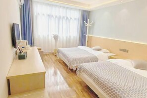 Quarto de hotel com duas camas, uma escrivaninha, uma cadeira e uma janela grande com cortinas.