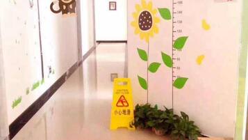Um corredor com um aviso de segurança, uma régua de altura e uma planta em vaso.