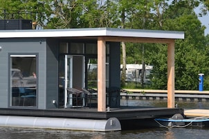 Uma estrutura moderna flutuante com deck coberto, portas de vidro e área de estar ao ar livre.