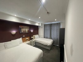 Quarto de hotel com duas camas, uma mesa de cabeceira, abajur, televisão e um quadro na parede.
