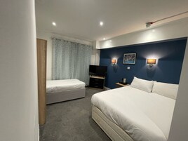 Quarto de hotel com duas camas, televisão, escrivaninha e luminárias fixadas na parede.