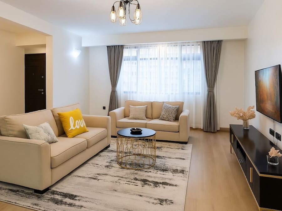 Uma sala de estar moderna com dois sofás, uma mesa de centro, uma TV e uma janela grande com cortinas.