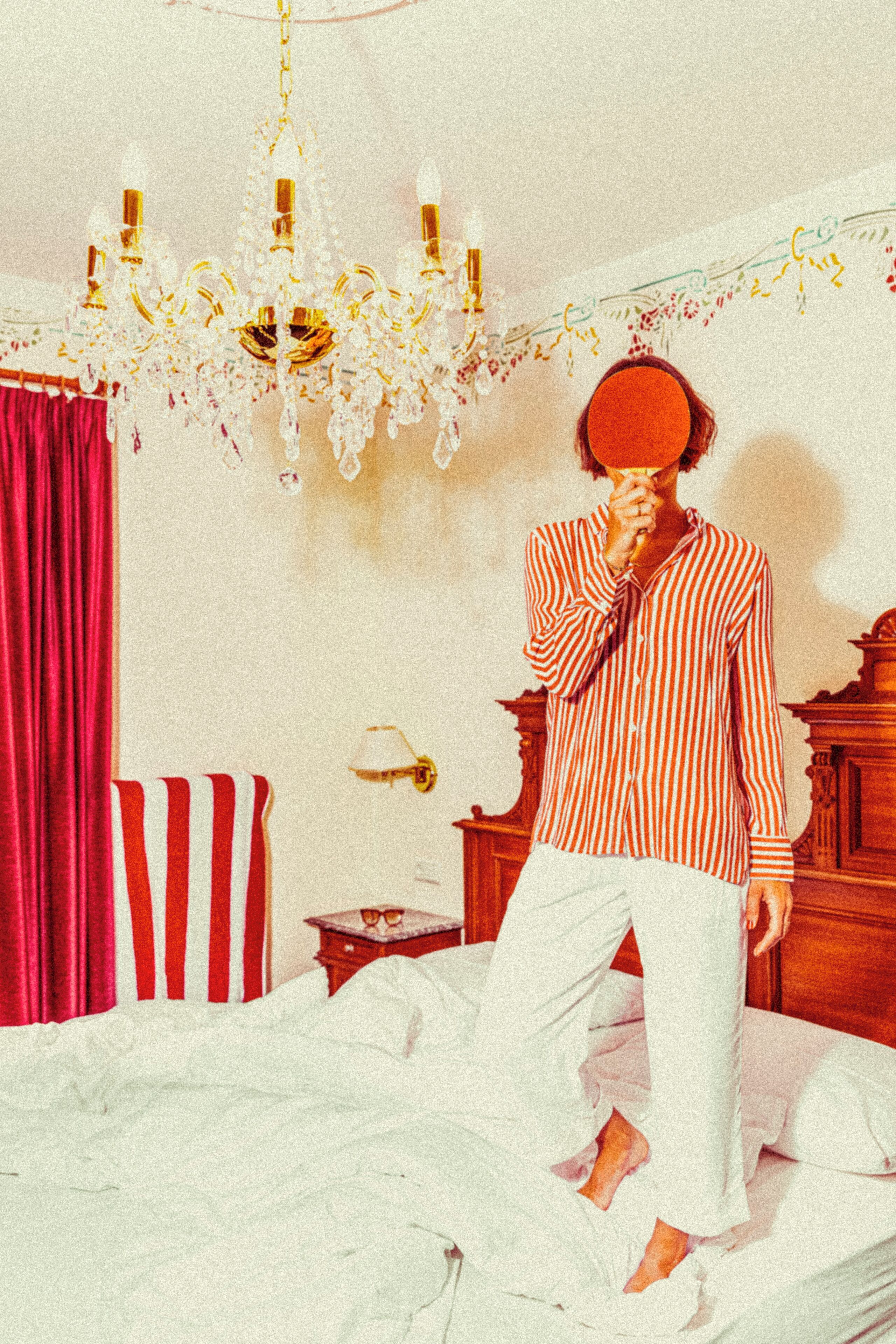 Um quarto com uma cama, um candelabro, uma cortina vermelha e uma camisa listrada.