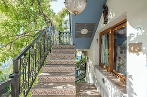 Uma escadaria com grades ornamentadas e degraus estampados, que leva a um quarto com uma grande janela e uma luminária decorativa no teto.