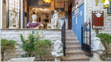 Fachada de edifício com estátuas clássicas, uma porta azul e uma placa com a inscrição 'casa Roma'.