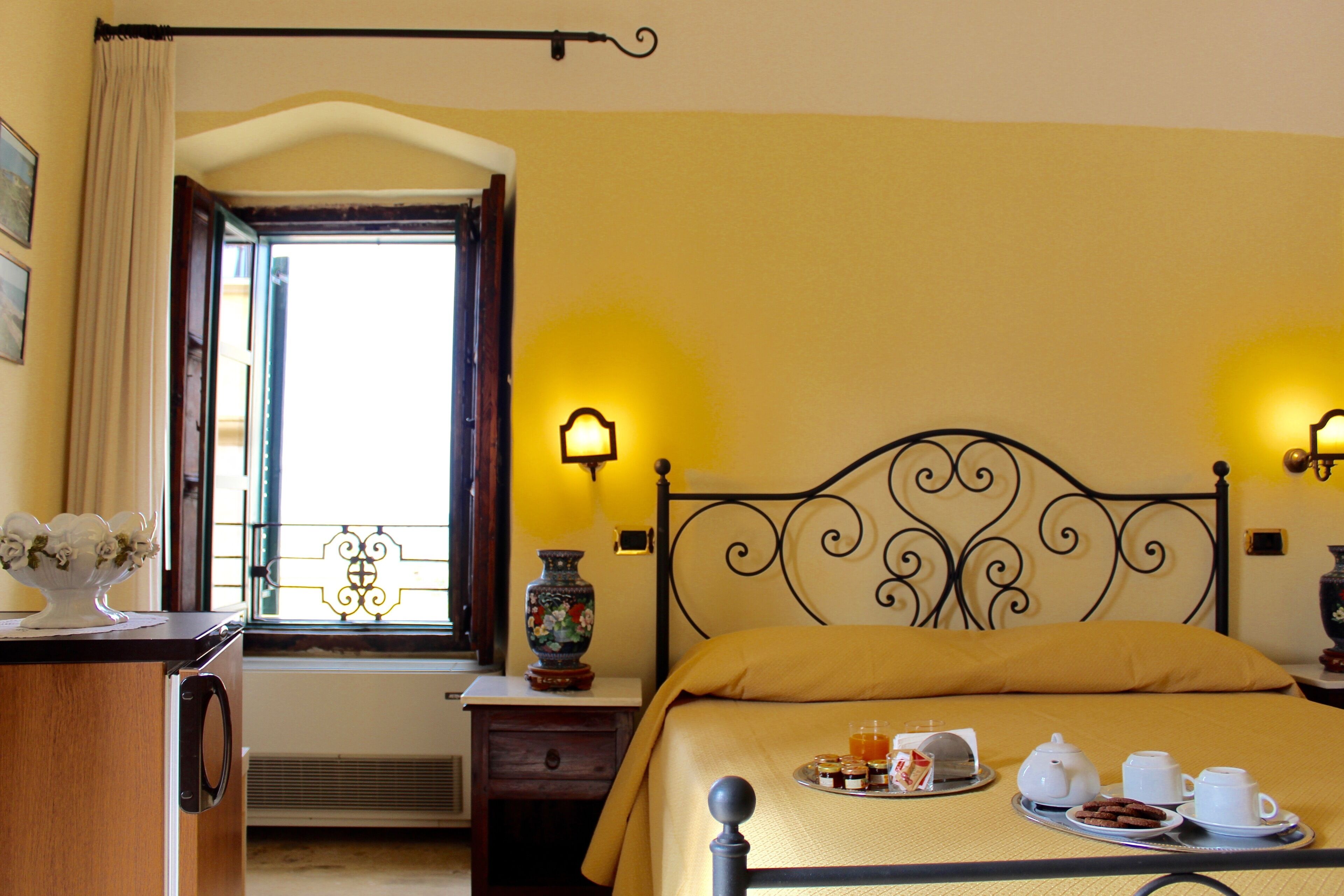 Quarto de hotel com cama, mesa de cabeceira e janela com cortinas.