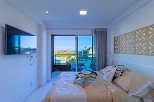 Quarto de hotel com cama, televisão fixada na parede e varanda com vista para a paisagem.