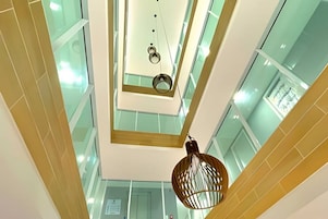 Interior moderno com teto alto, guarda-corpos de vidro e luminária pendente.