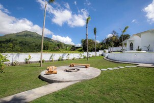 Um jardim ajardinado com lareira de concreto, bancos de madeira e um edifício branco com uma grande janela.