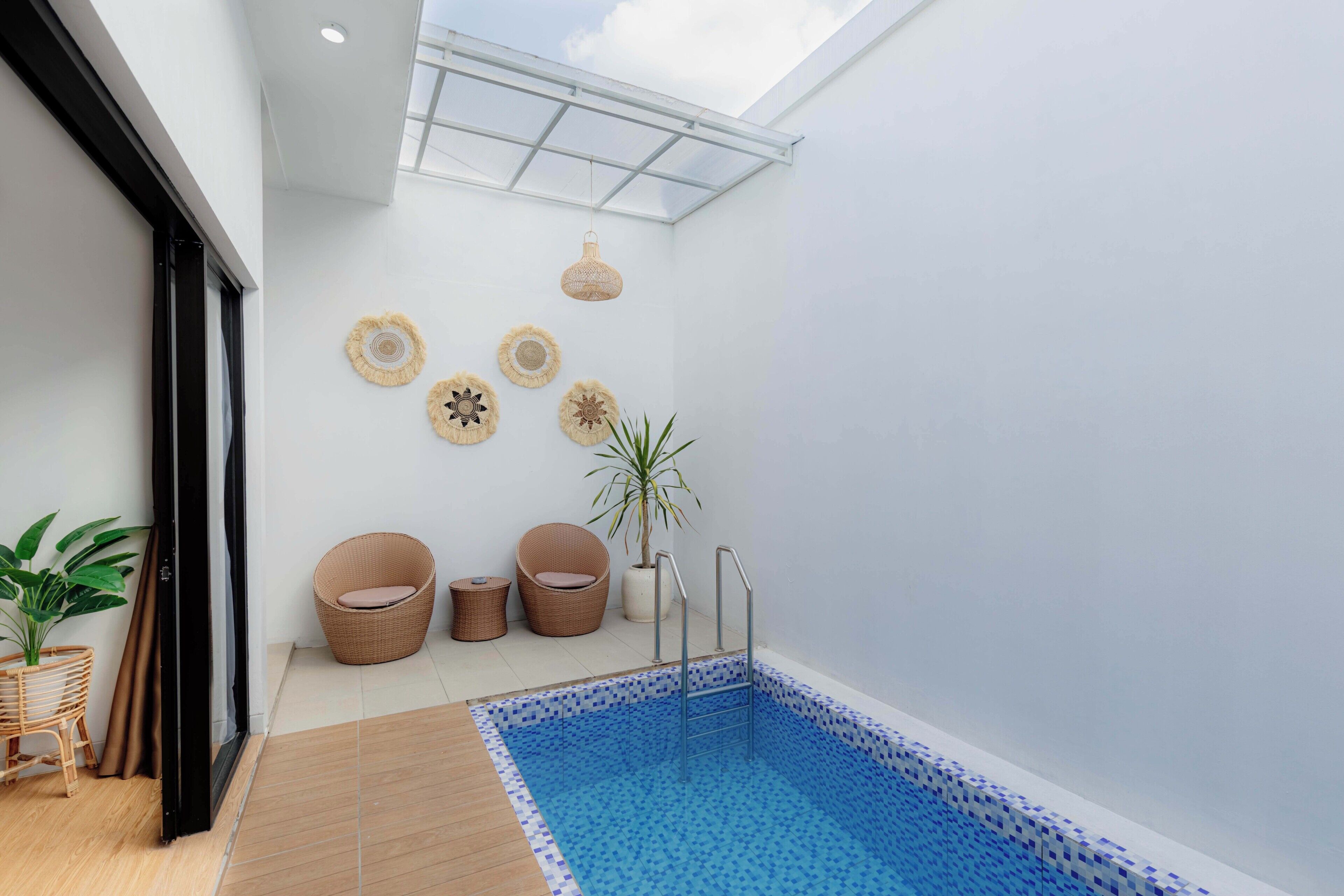 Pequena piscina interior com teto de vidro, rodeada por móveis de vime e obras de arte decorativas na parede.