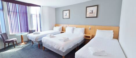 Quarto de hotel com três camas, uma mesa redonda e uma cadeira.
