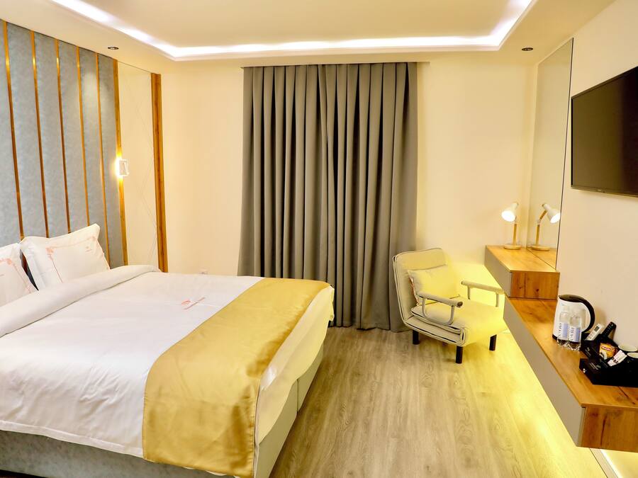 Quarto de hotel com uma cama, uma escrivaninha com cafeteira, uma cadeira, um espelho e uma televisão.