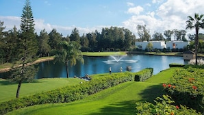 Um campo de golfe com um lago, árvores e um edifício ao fundo.