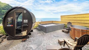 Área de hidromassagem com um barril de madeira, assentos e vista para o mar.