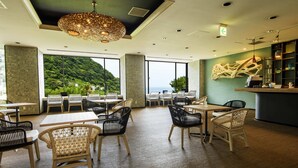 Um restaurante moderno com cadeiras de vime, grandes janelas e vista para o mar.
