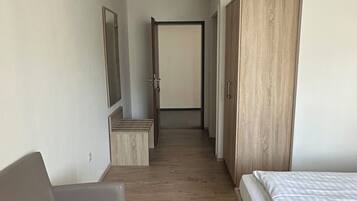 Quarto de hotel com cama, escrivaninha, cadeira, guarda-roupa e porta que dá para outro espaço.