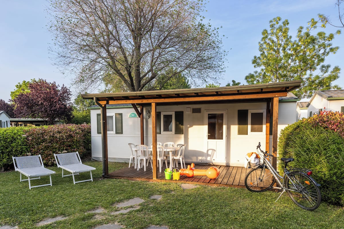 Um pequeno pátio externo com pérgola de madeira, uma mesa e cadeiras, e uma bicicleta.