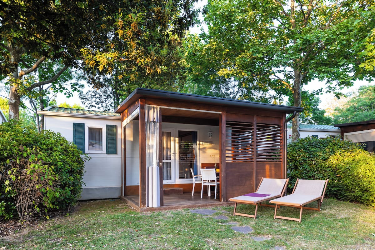Uma casa pequena e moderna com varanda coberta, área de refeições e duas poltronas.