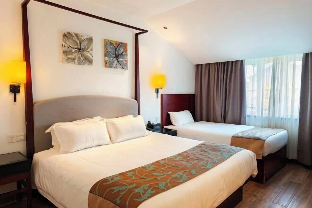 Quarto de hotel com duas camas, uma janela grande com cortinas e obras de arte nas paredes.