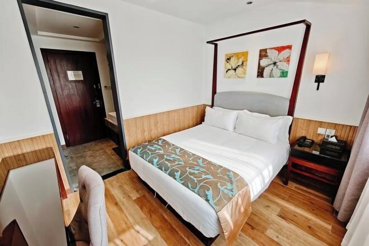 Quarto de hotel com cama, escrivaninha, cadeira, mesa de cabeceira e duas luminárias fixadas na parede.