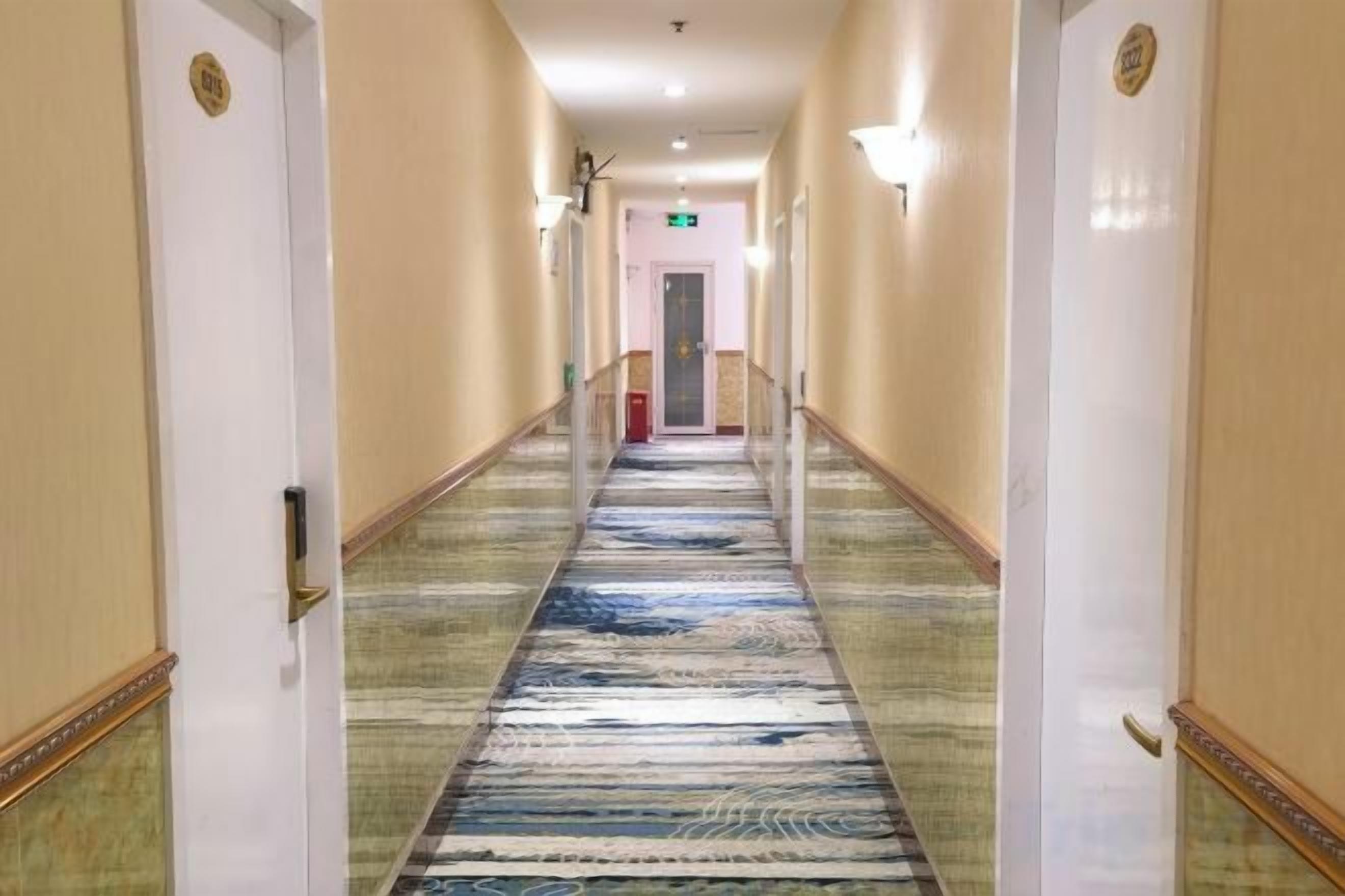 Corredor de hotel com piso carpetado, portas em ambos os lados e luminária na parede.