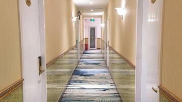 Corredor de hotel com piso carpetado, portas em ambos os lados e luminária na parede.