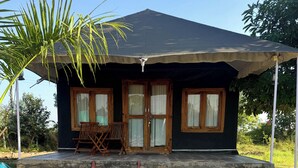 Uma casa pequena com varanda, duas cadeiras de madeira e um banco.
