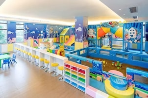 Espaço infantil com diferentes brinquedos e área de descanso com banquinhos amarelos.