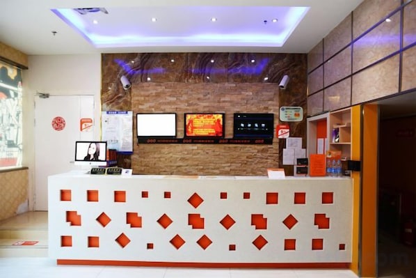 Balcão de recepção com design moderno, um painel de exibição digital e uma placa fixada na parede.