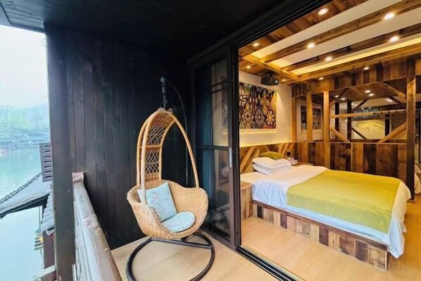 Quarto com cama, cadeira suspensa e vista para um corpo d'água.