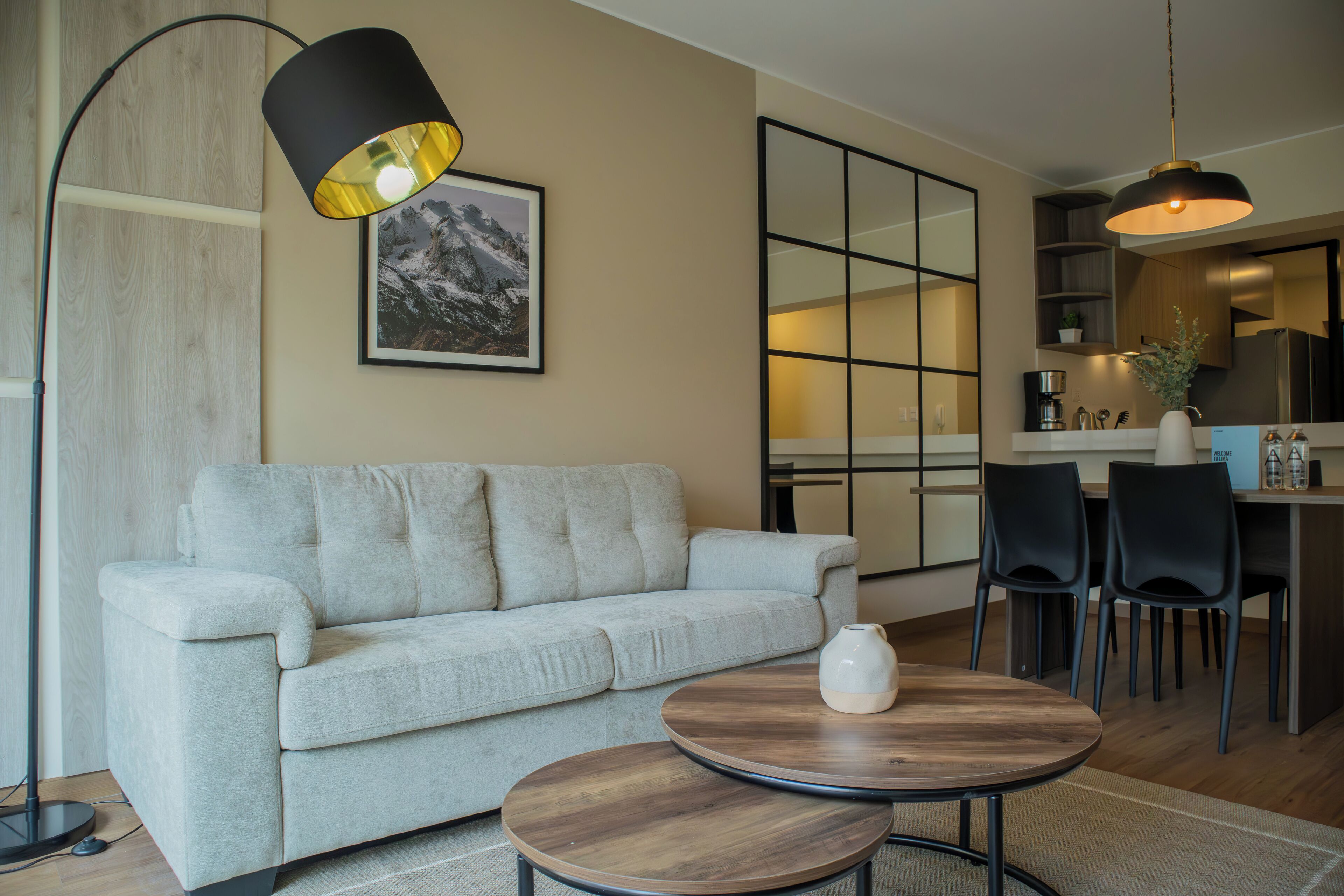 Uma sala de estar moderna com um sofá, duas mesas redondas, uma cafeteira e um espaço de jantar com cadeiras.