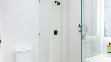 Uma casa de banho moderna com chuveiro em cabine de vidro, sanita branca e lavatório com espelho.