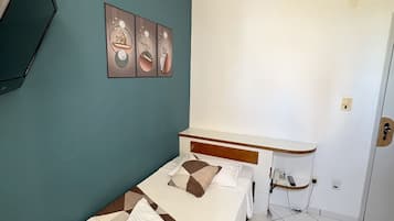 Quarto individual com uma cama, uma escrivaninha, televisão de tela plana e obras de arte na parede.