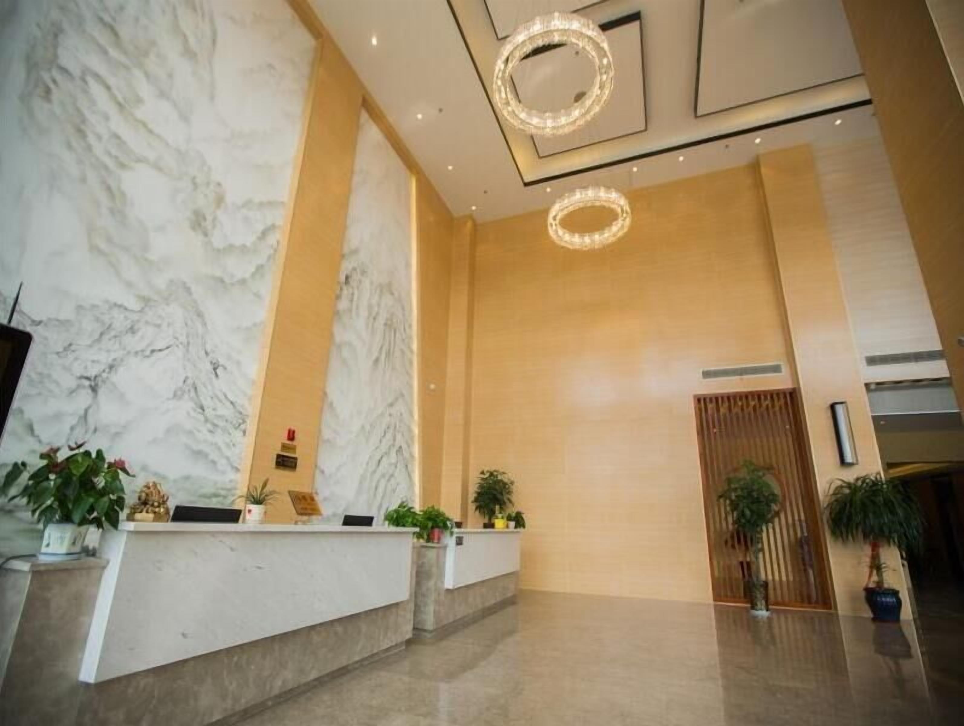 Uma área de recepção moderna com paredes de mármore, balcão de atendimento e plantas em vasos.