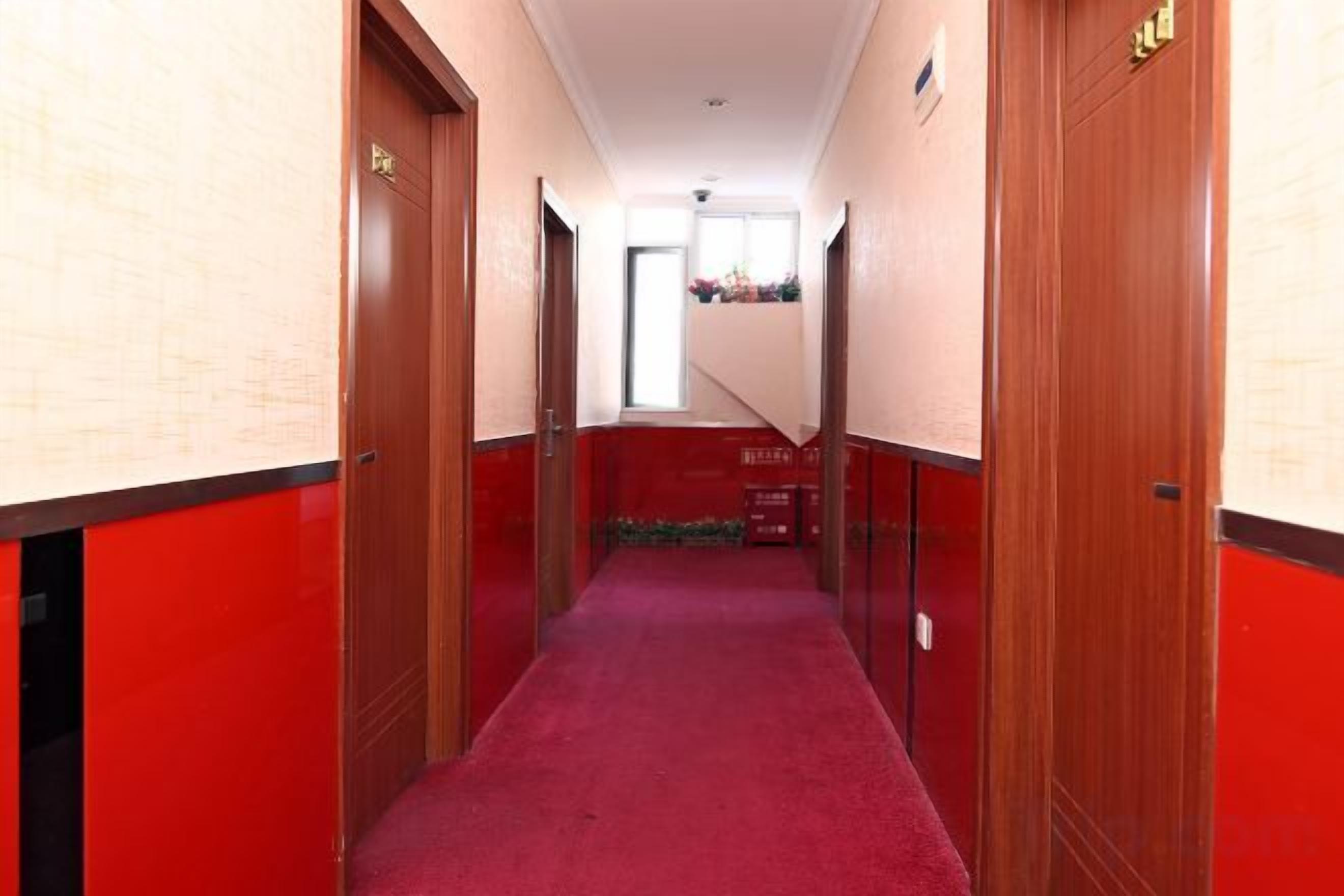 Corredor com paredes e portas vermelhas, chão coberto por carpete e escada ao fundo.