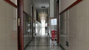 Um corredor com portas de vidro, uma caixa de correio vermelha e piso de azulejos.