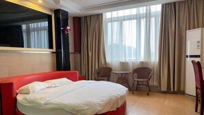 Quarto de hotel com cama vermelha, uma mesinha com cadeiras, televisão e frigorífico.