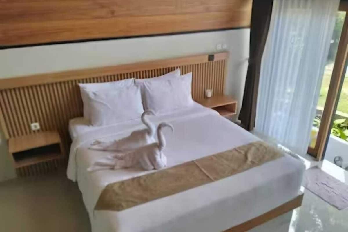 Cama bem arrumada com cabeceira de madeira, mesa de cabeceira e janela com cortinas.