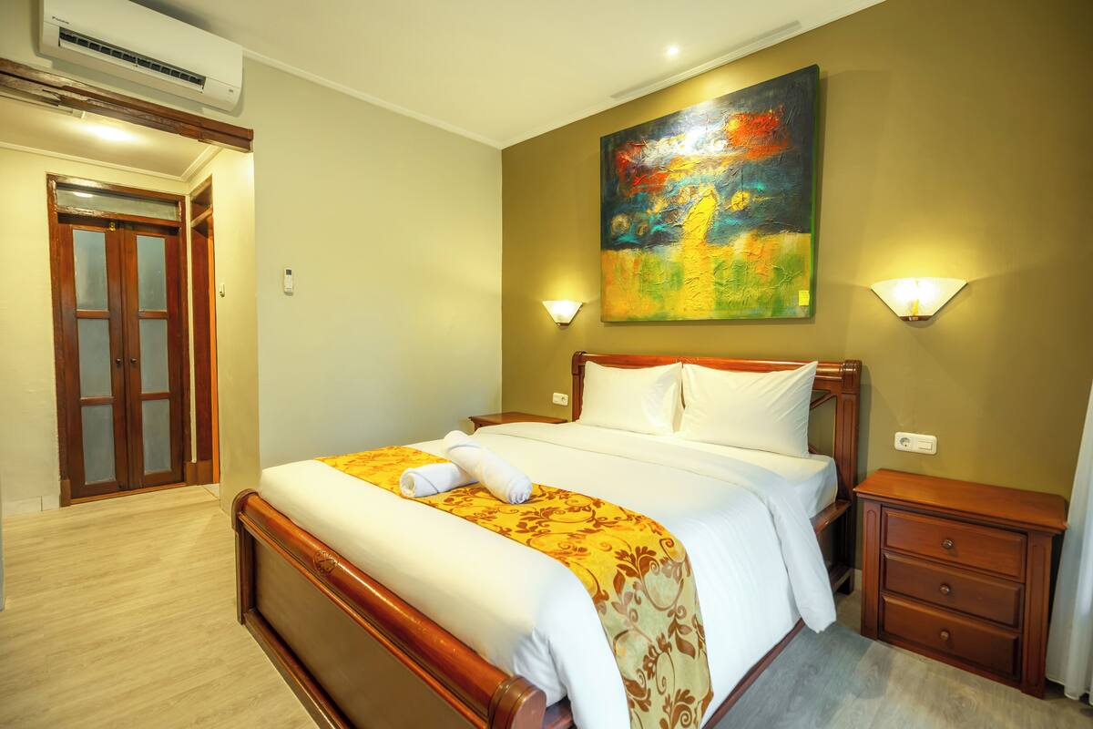 Quarto de hotel com cama de madeira, um quadro na parede e duas luminárias fixadas na parede.