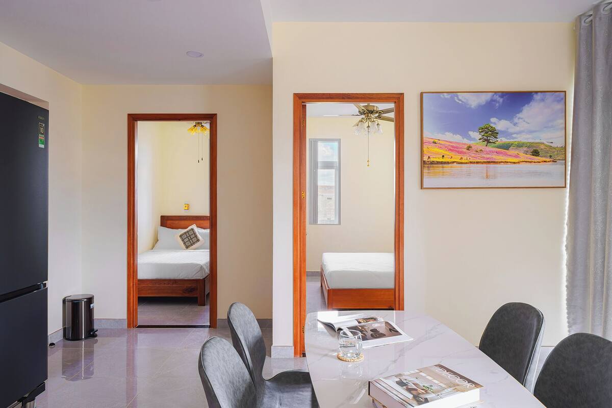 Quarto de hotel com cama, escrivaninha com cadeiras, televisão e um quadro na parede.