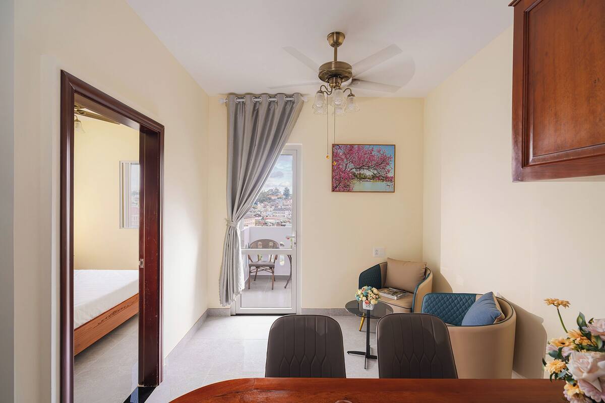 Quarto com cama, mesa de jantar, sofá, ventilador de teto, quadro e vista para o exterior.