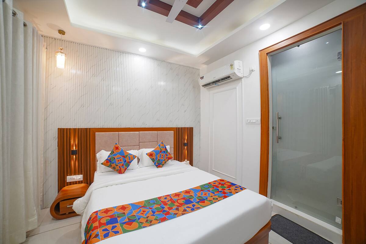 Quarto de hotel com uma cama grande, cabeceira de madeira, chuveiro com porta de vidro e uma luminária no teto.